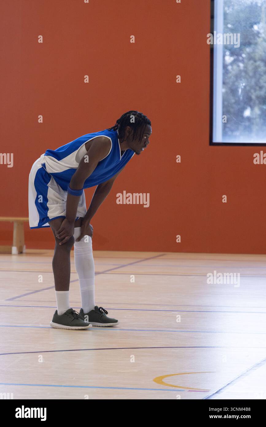 African american male basketball player bending forward on gym floor ...