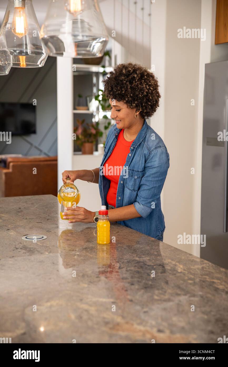African american adult woman pouring orange juice from pitcher into ...