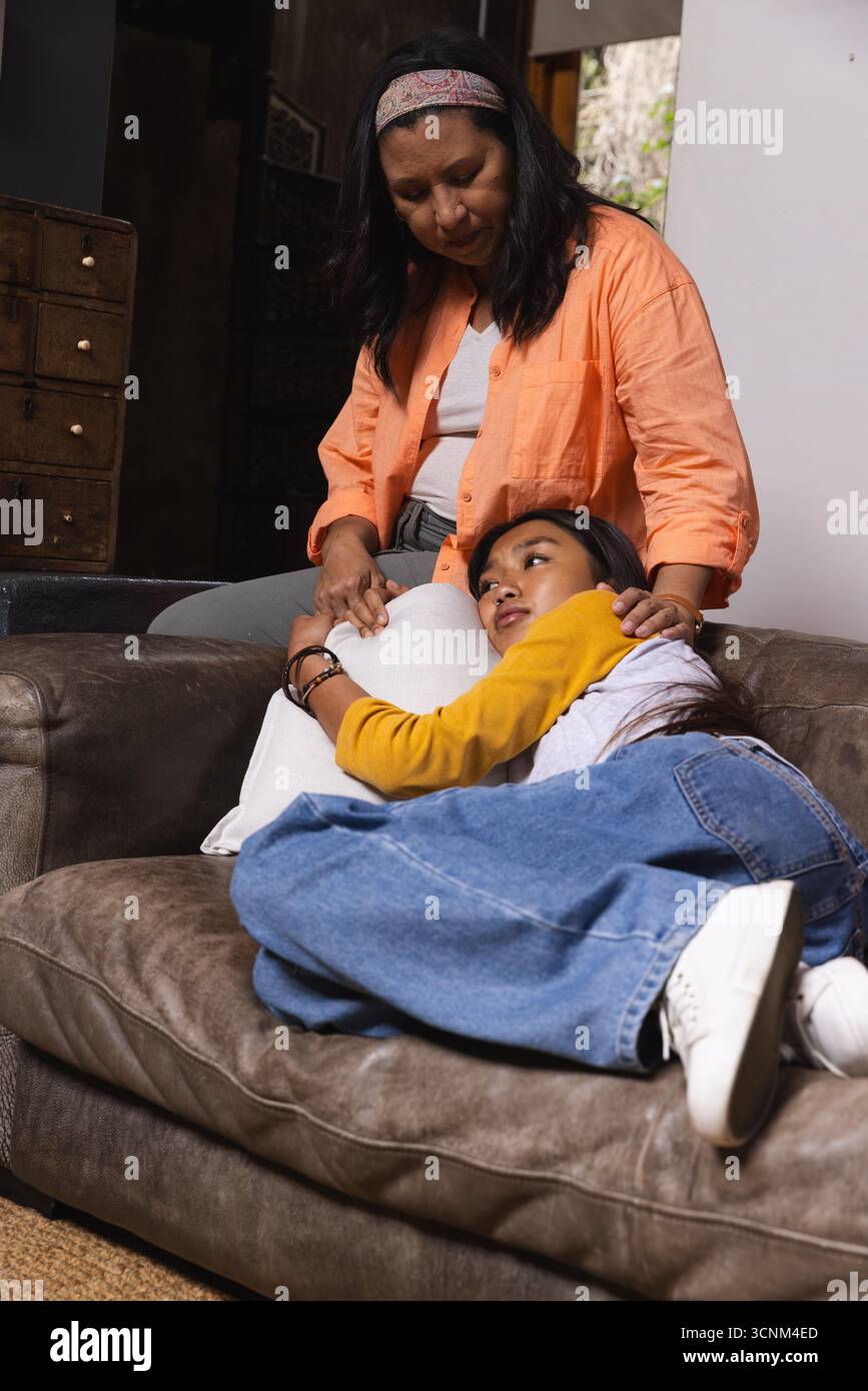 Mother holding belly and daughter resting across lap hugging stomach on ...