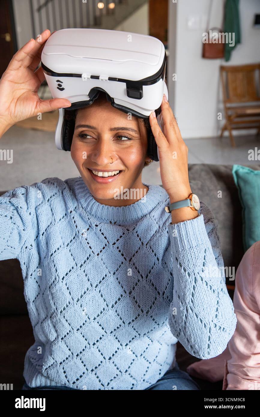 Indian woman raising vr headset overhead on sofa in living room with ...