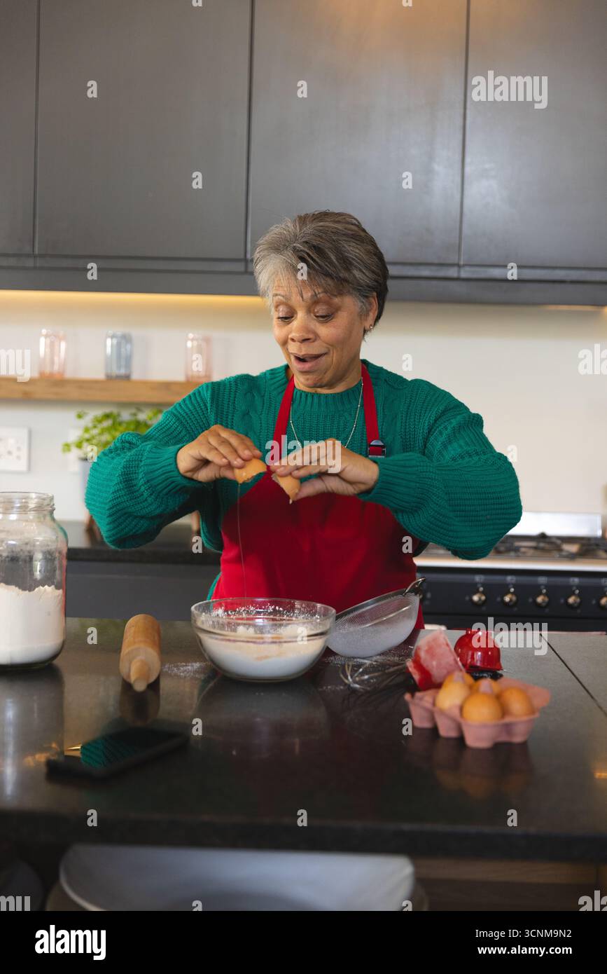 Senior African American cook wearing red apron cracking egg into bowl ...
