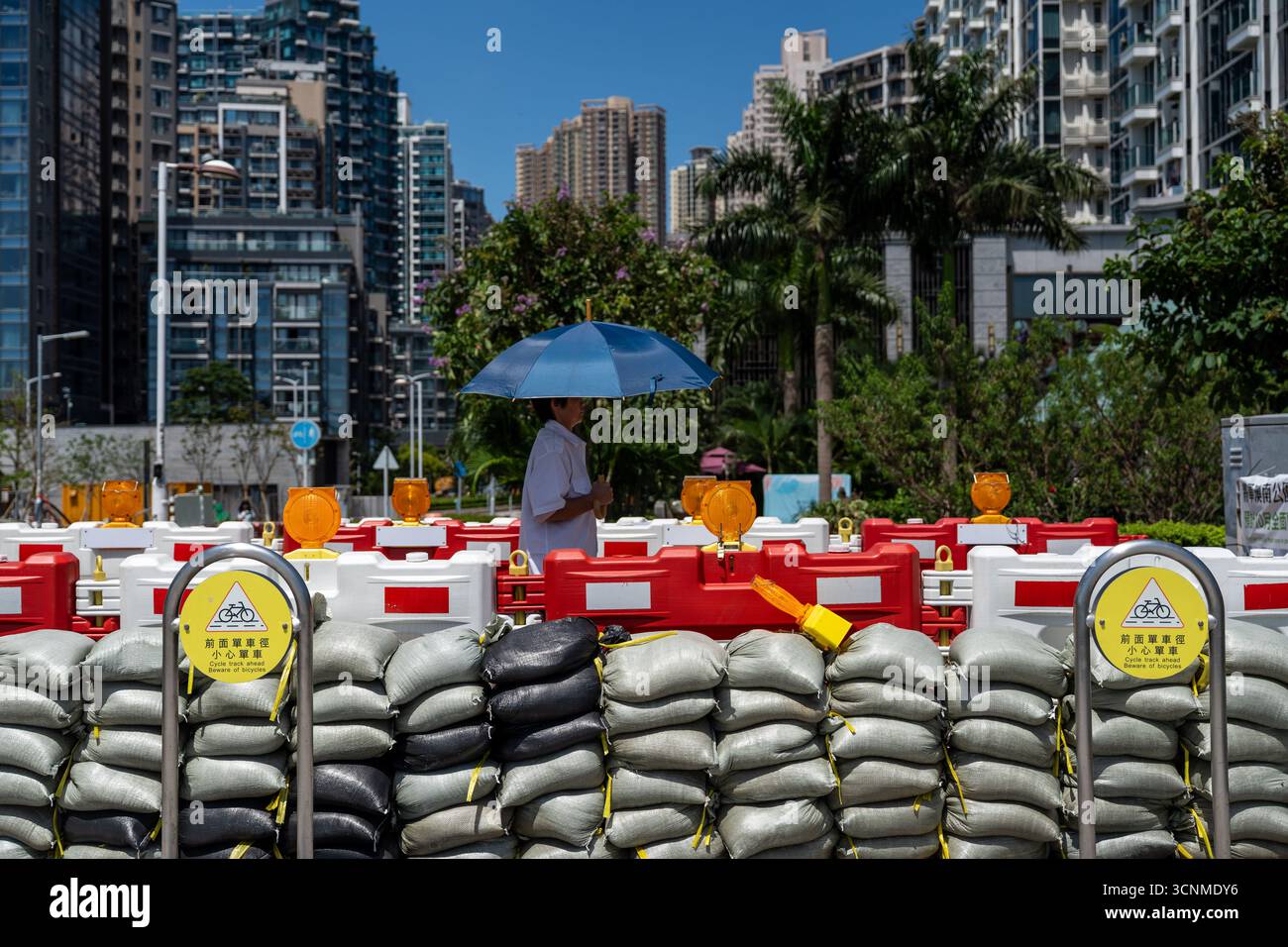 A person holding an umbrella walks pass barricades filled with water ...
