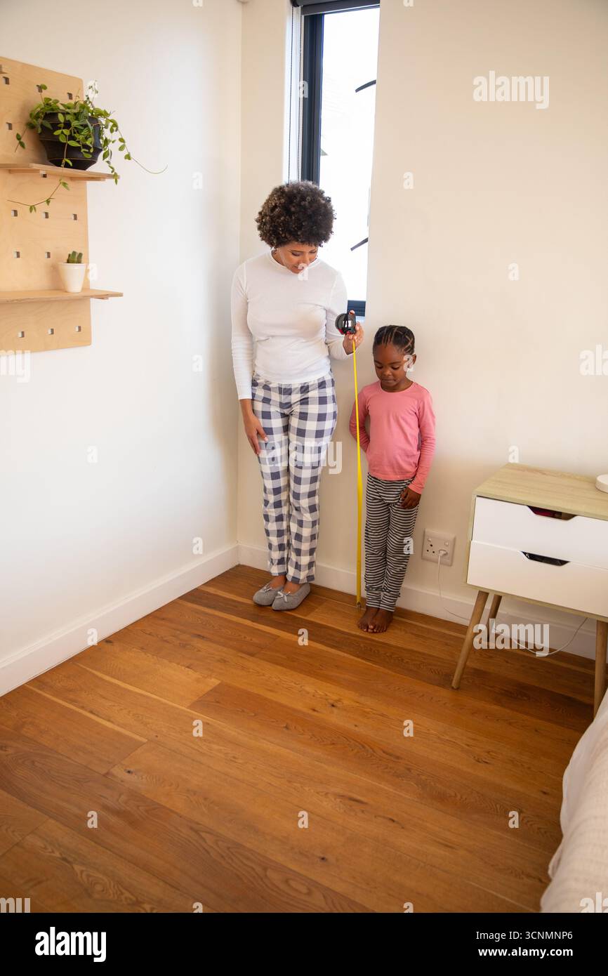 African american mother with daughter measuring child height at home by ...