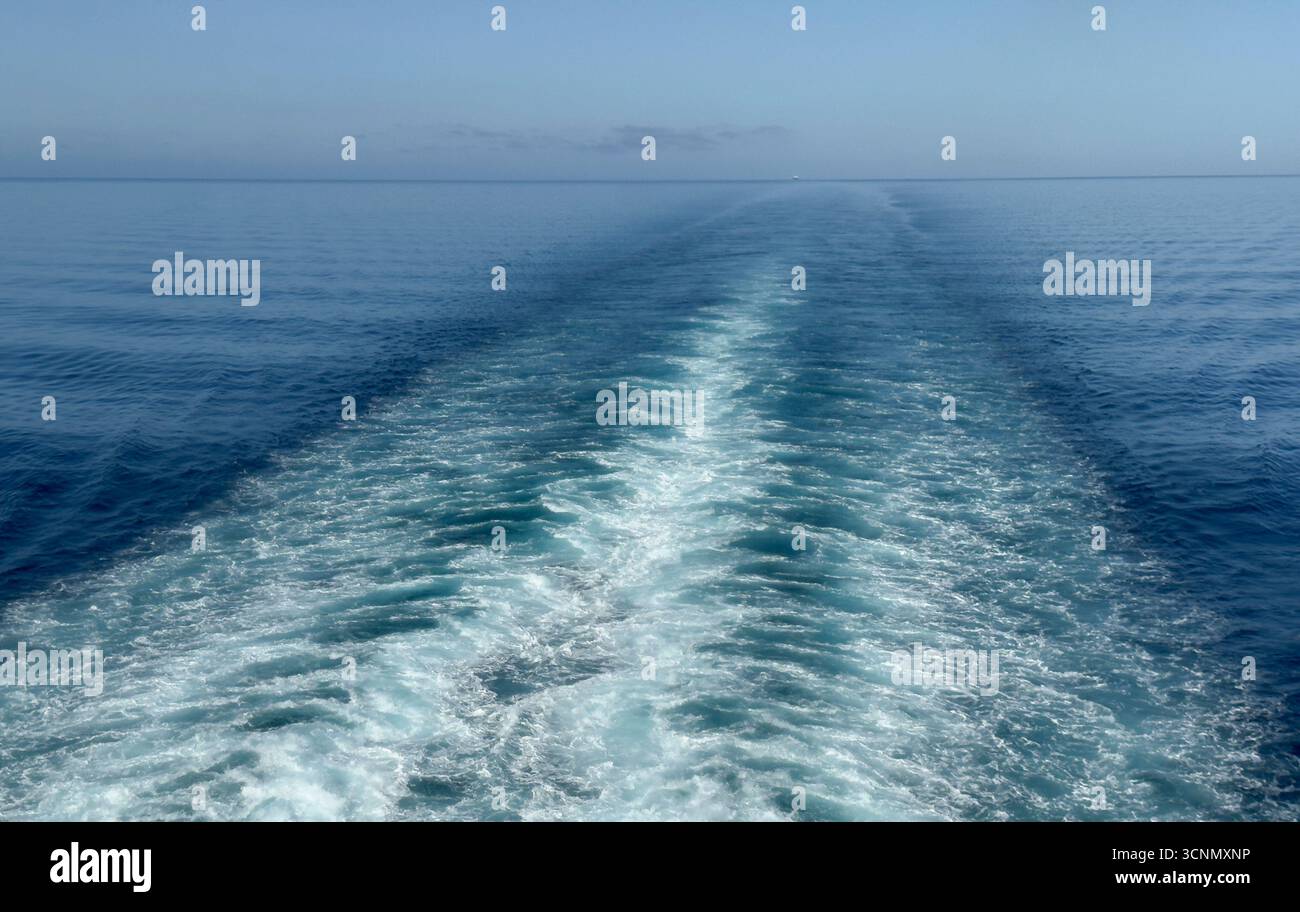 Tranquil view of the vast blue ocean with a boat’s wake stretching into ...