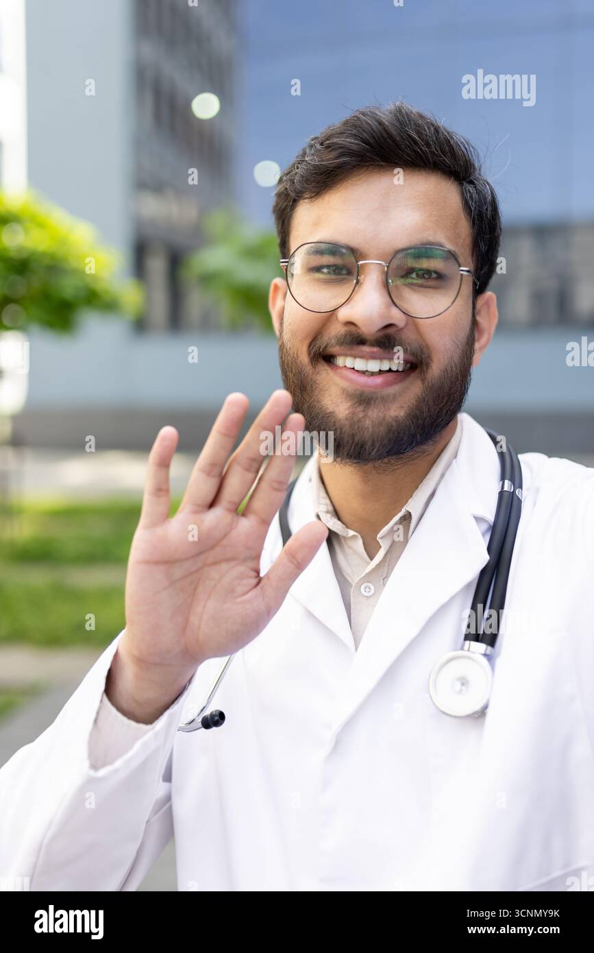 Indian doctor in white coat with stethoscope, smiling and waving at ...