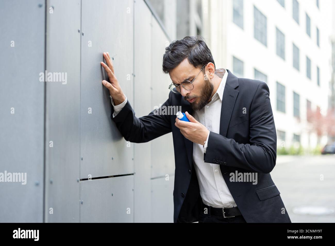 Businessman in suit leans against urban wall, using inhaler to ease ...