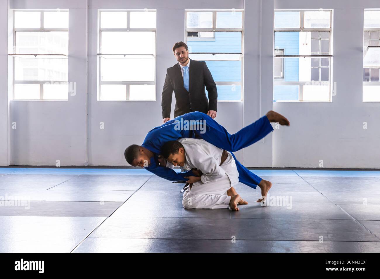Diverse judo group performing judo throw in dojo on mats with blue and ...