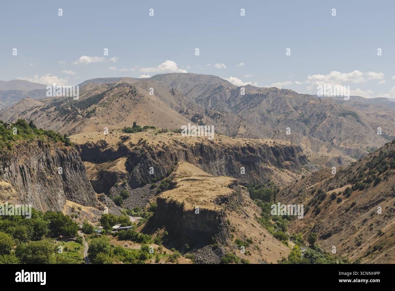 View of rugged cliffs dropping into a lush valley, under a vast sky ...