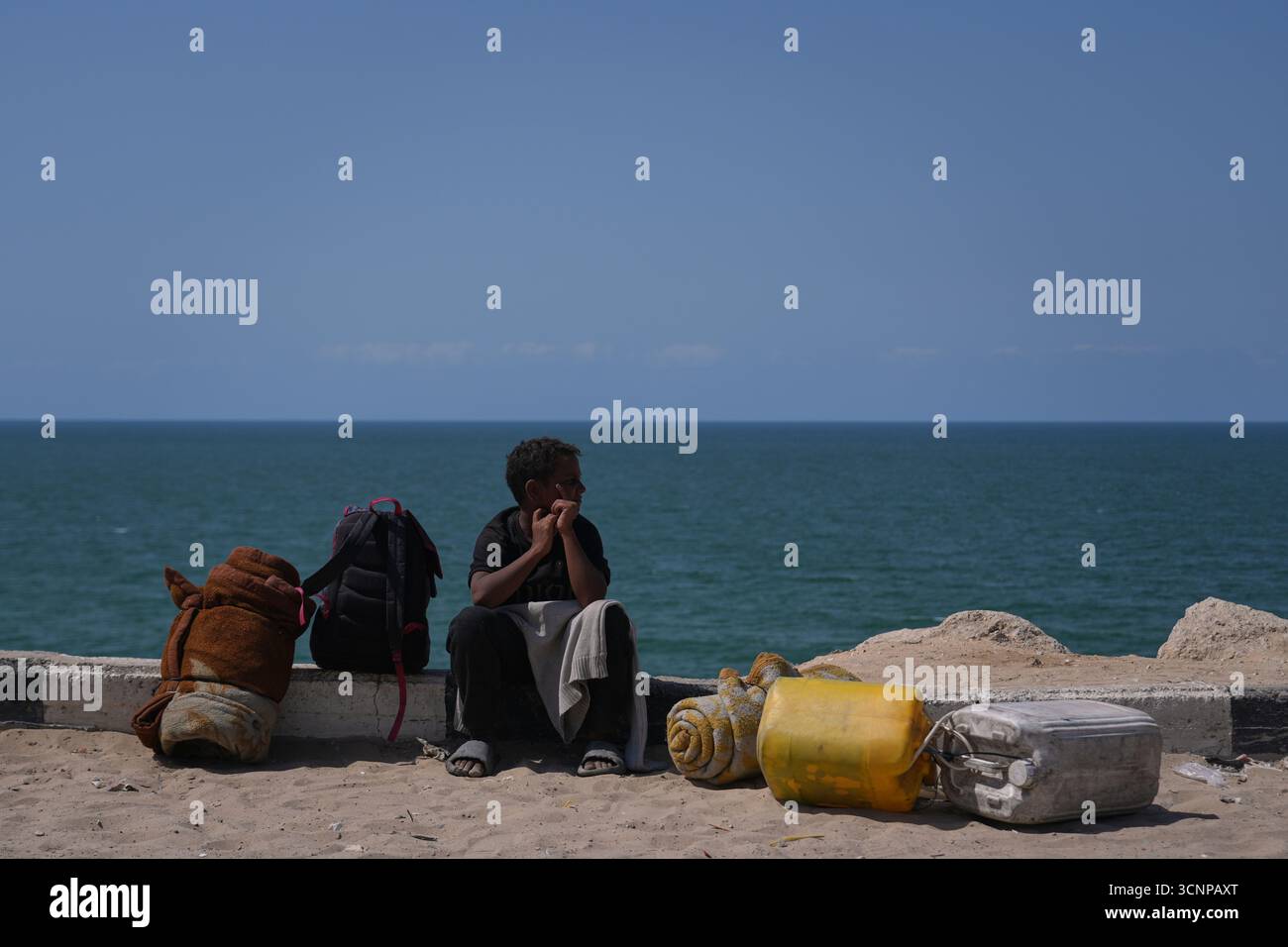 A displaced Palestinian youth sits on the curb after fleeing northern ...