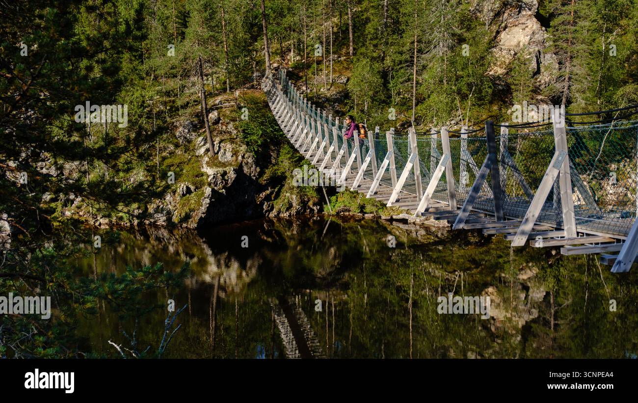 Two hikers cross a scenic suspension bridge over the tranquil waters of ...
