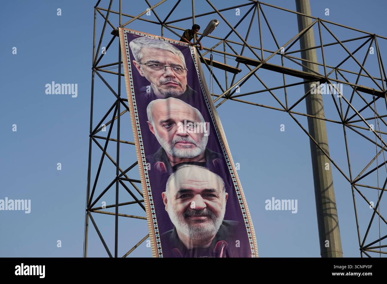 A worker hangs a banner showing portraits of the late Iranian armed ...