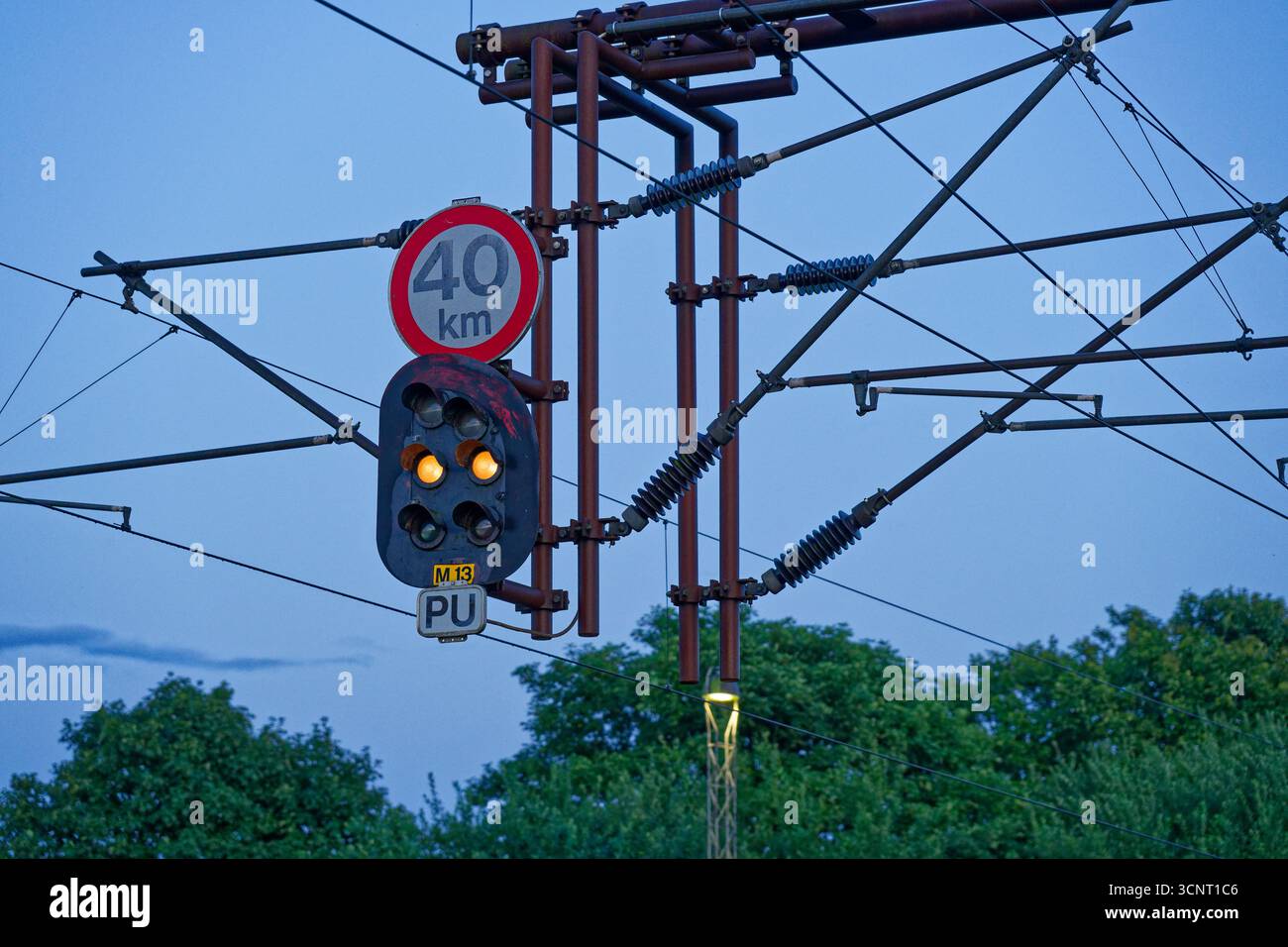 A suspended railway signal shows a steady yellow aspect with a speed ...