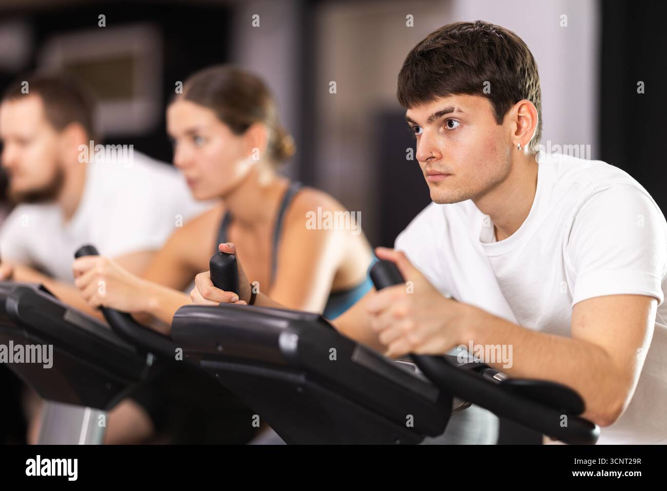 Focused guy works out with stationary bicycle during class at fitness ...