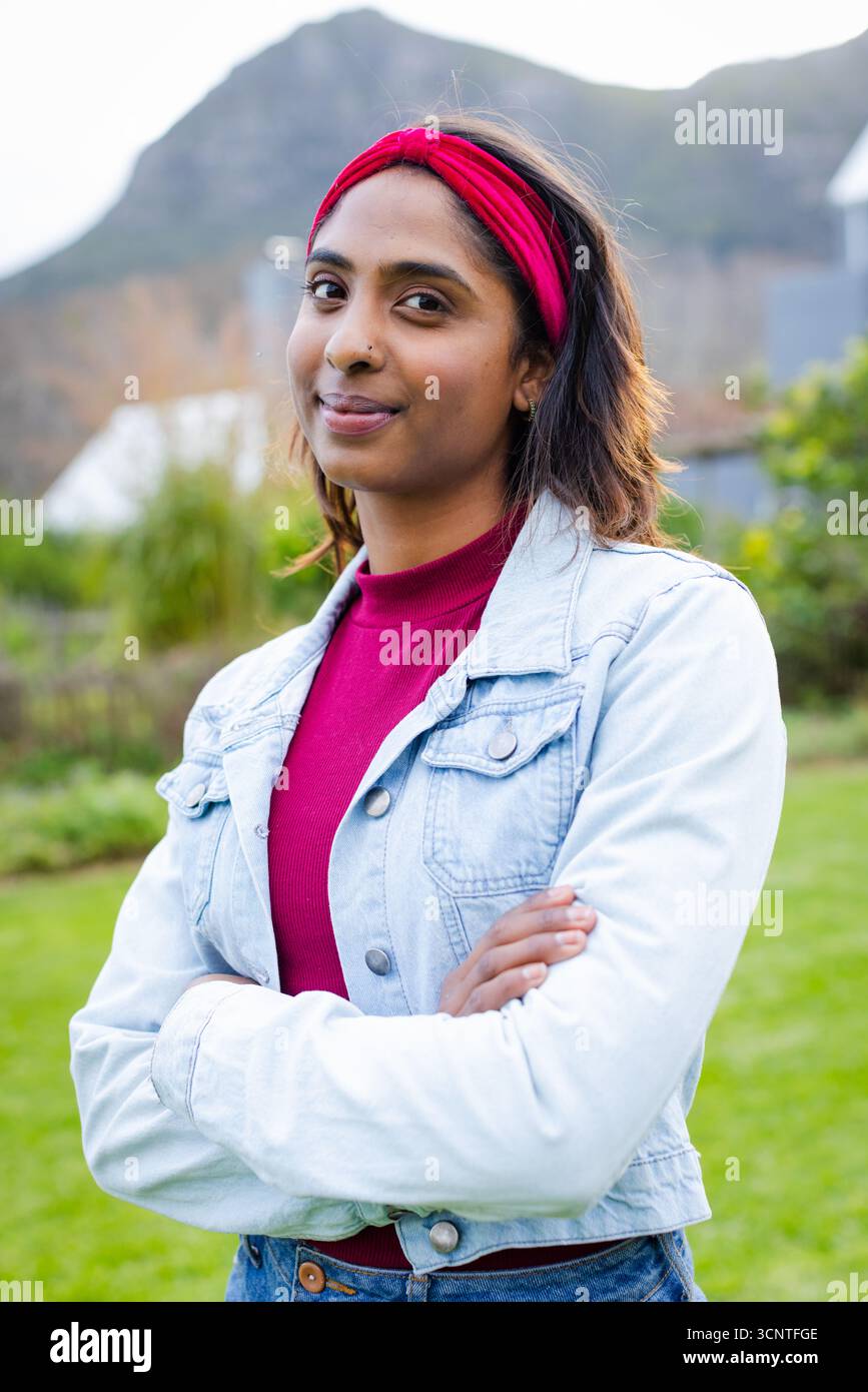 Indian woman standing with arms crossed in garden wearing red cloth ...