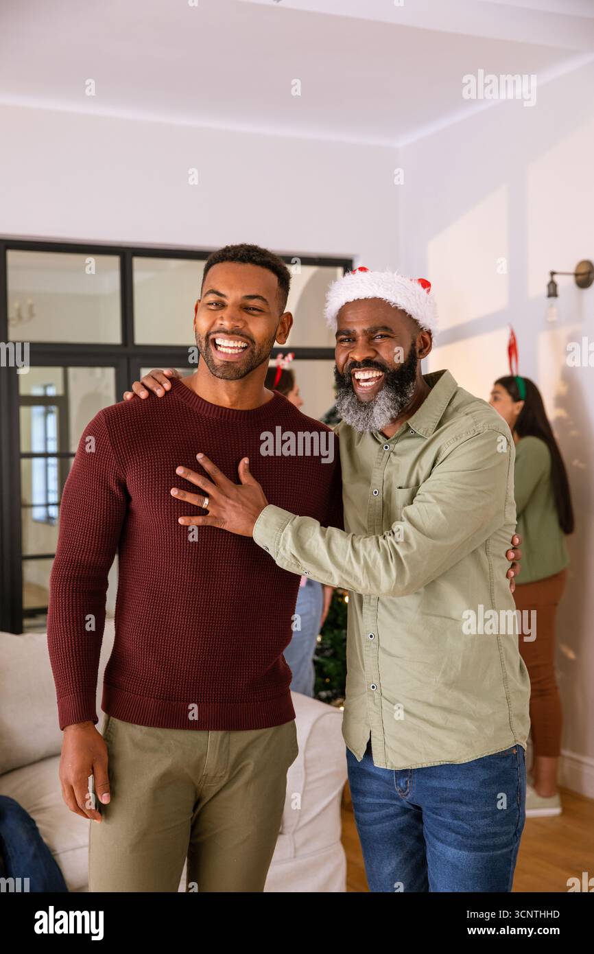 African American father and son standing hugging in living room wearing ...