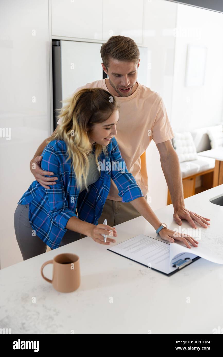 Couple signing papers over white kitchen countertop at home with ...