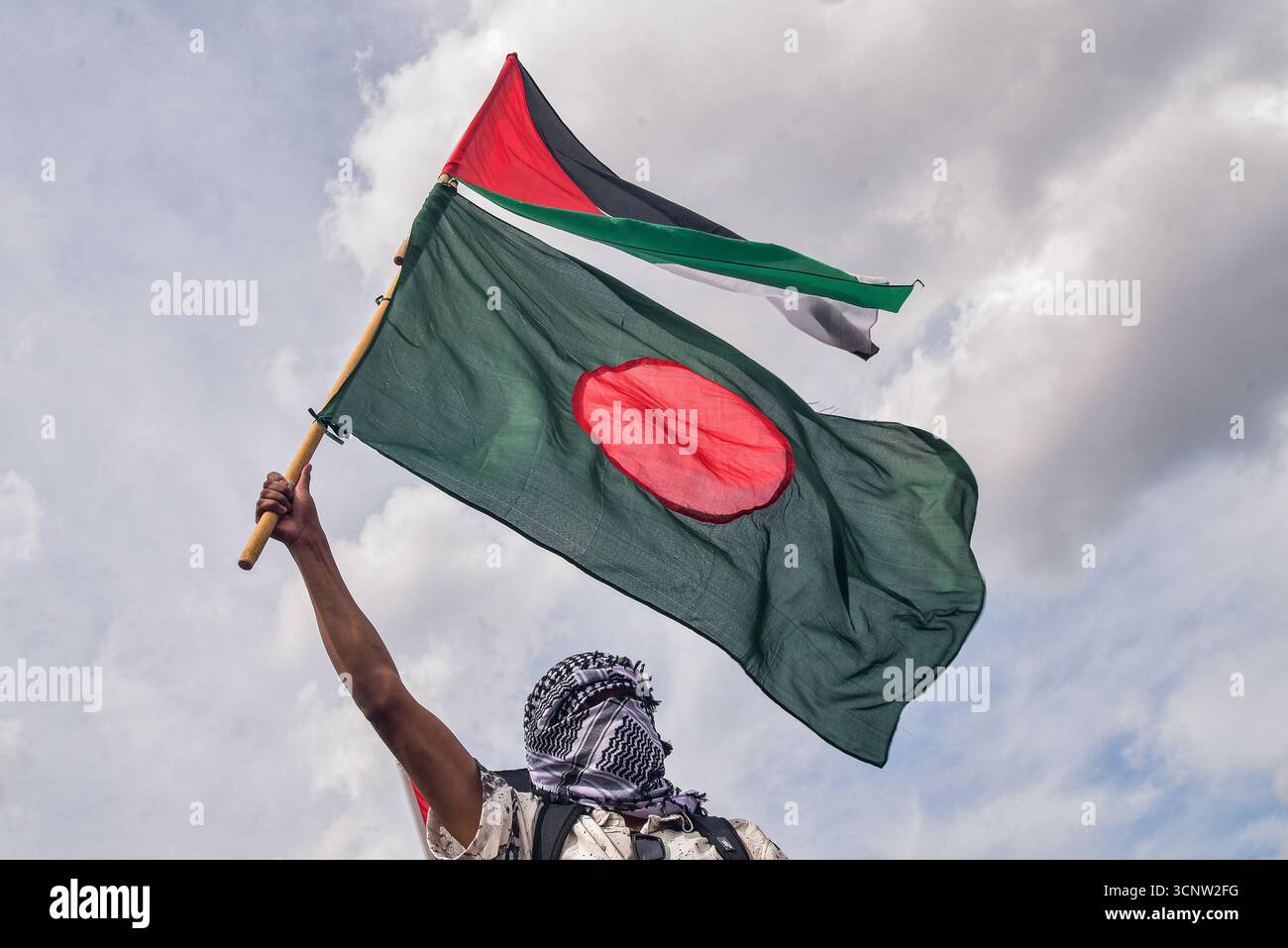 An activist wearing a keffiyeh waves Palestinian and Bangladeshi flags ...