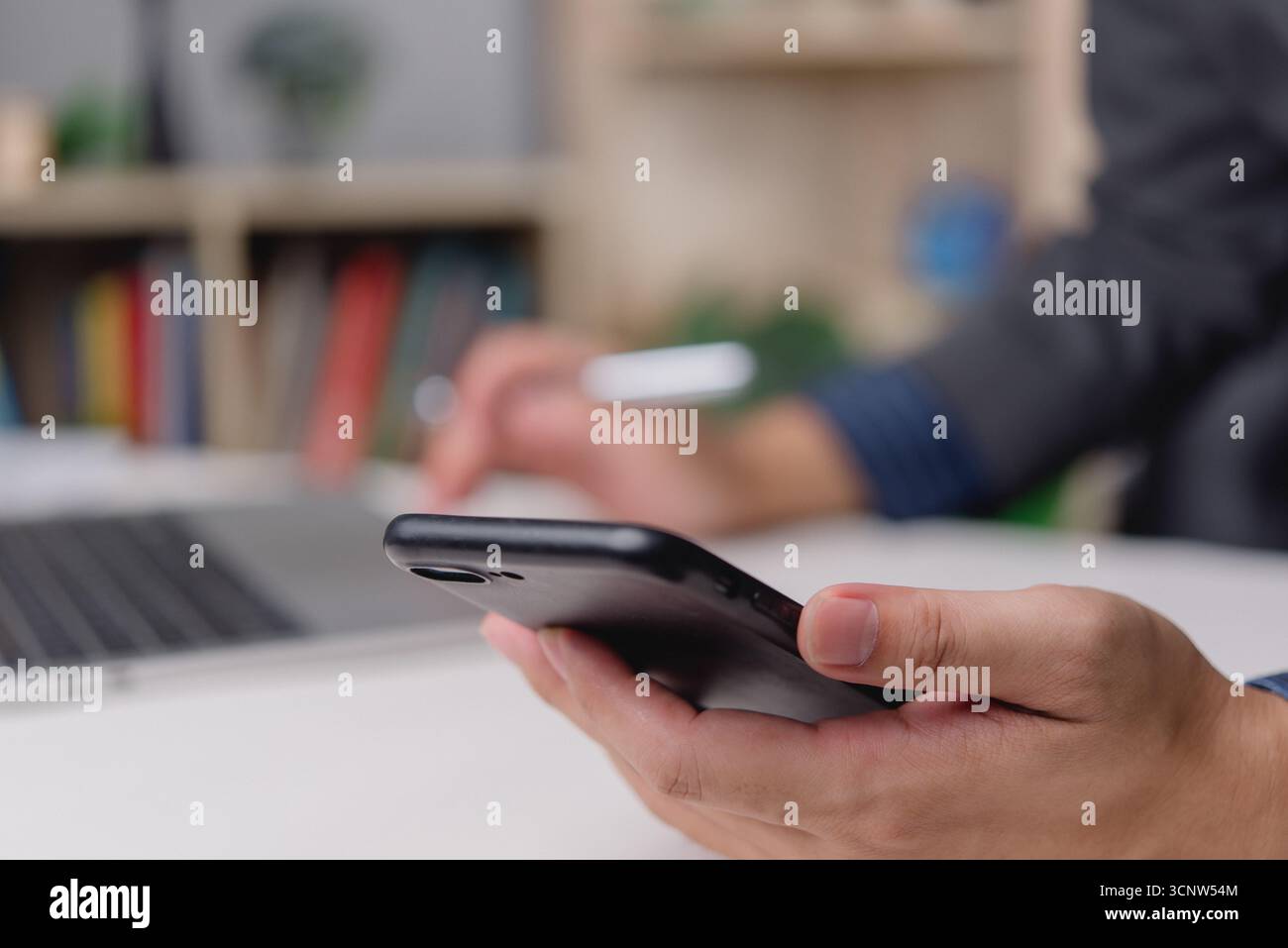 Hand holding smartphone with laptop in background. Concept of ...