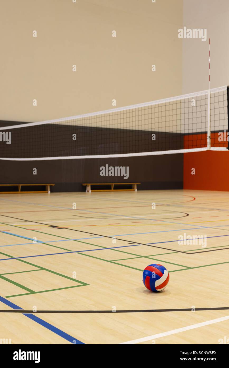 Multi-color volleyball resting on court floor under net beside benches ...