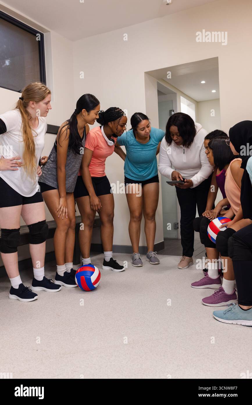Diverse female volleyball players gathering around coach showing ...