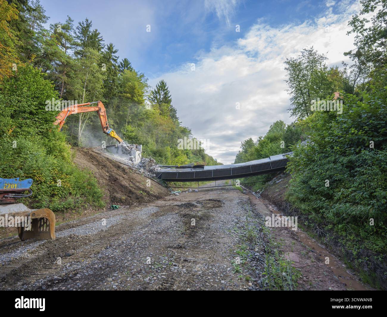 Two excavators tearing down a bridge on a gravel road, flanked by ...