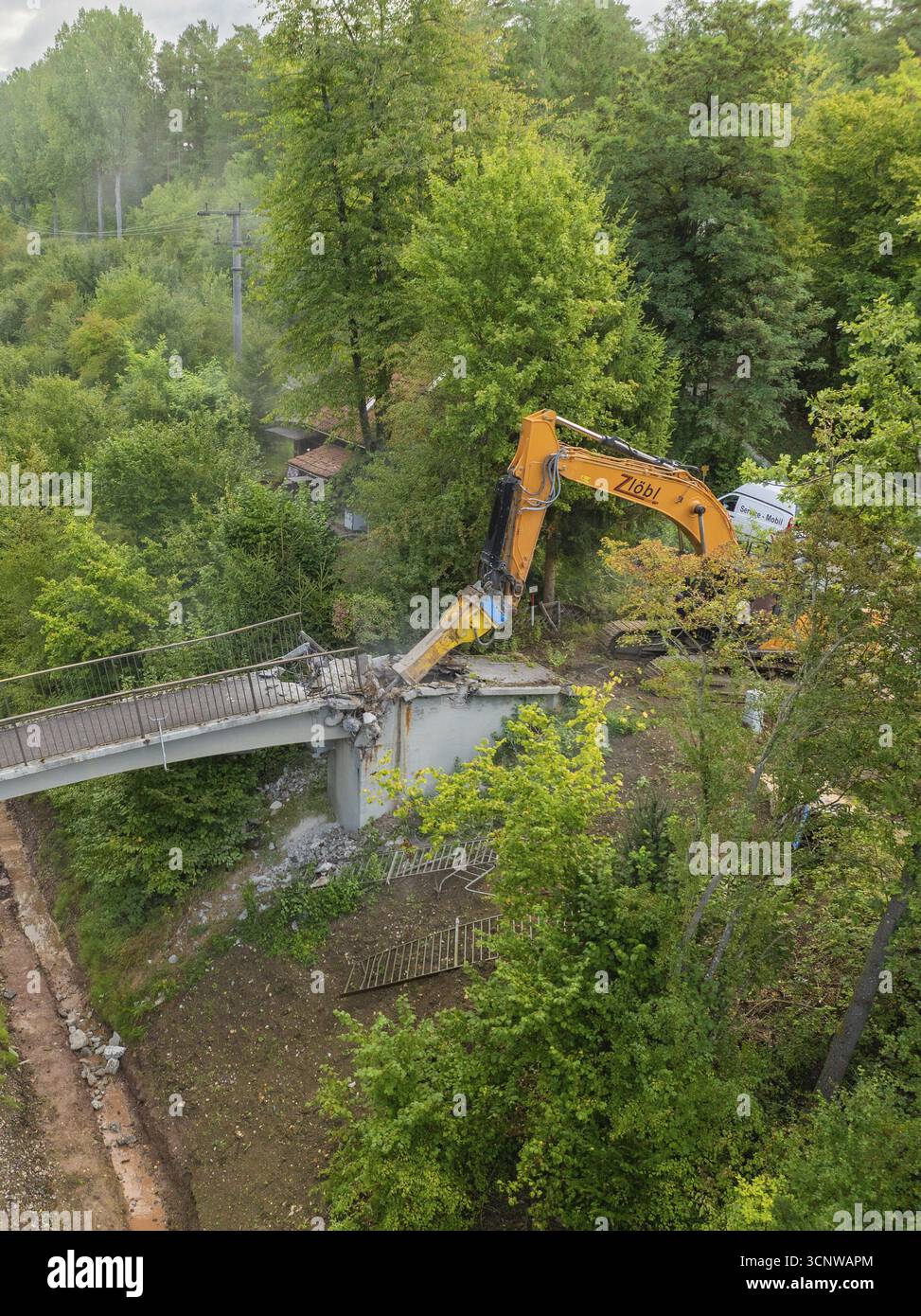 Excavator tears down part of a bridge in a green forest, an empty path ...