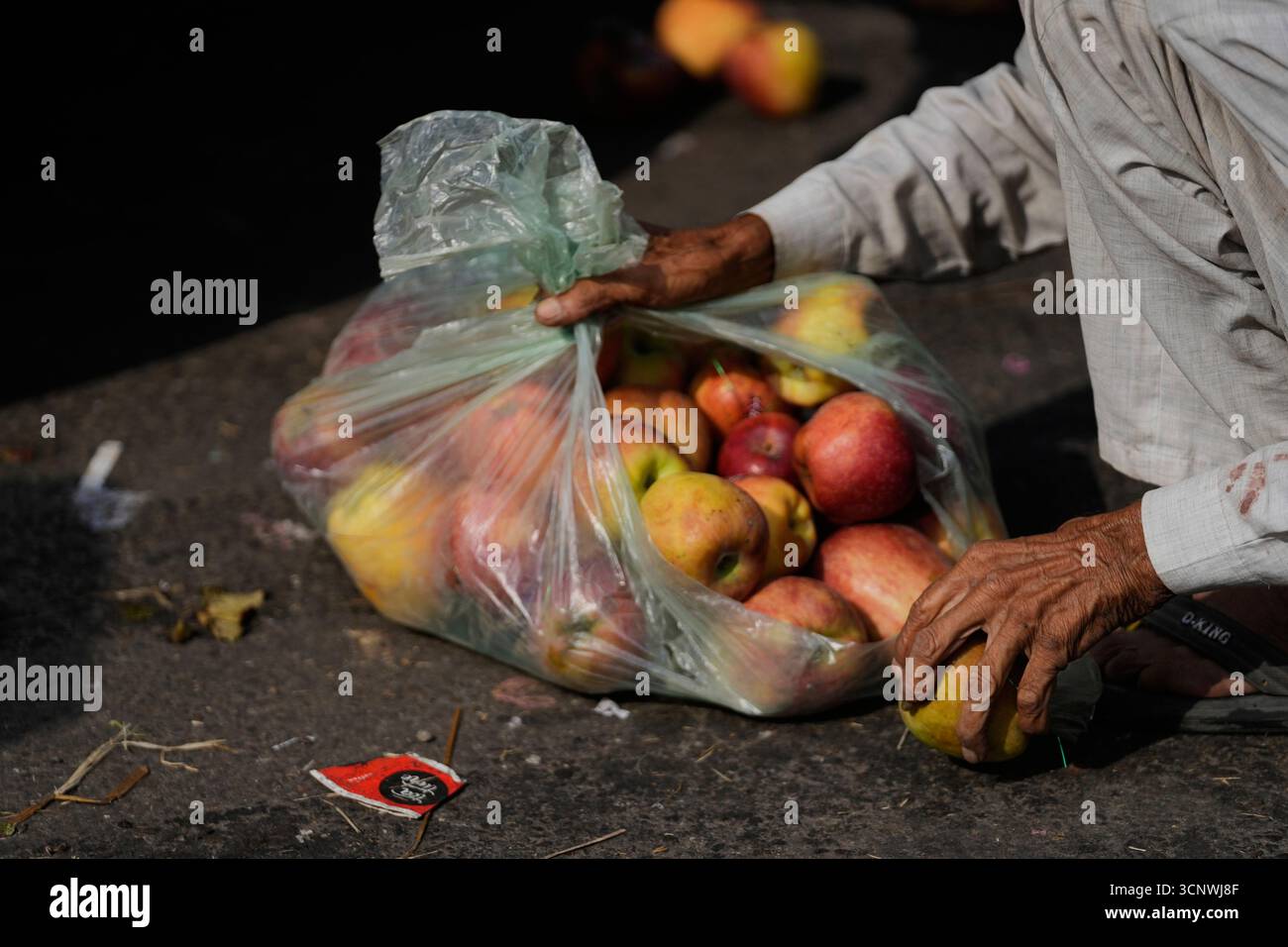 A man collects discarded rotten apple at a wholesale market as the ...