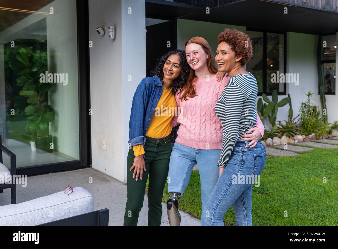 Diverse female friends hugging each other on concrete patio beside ...