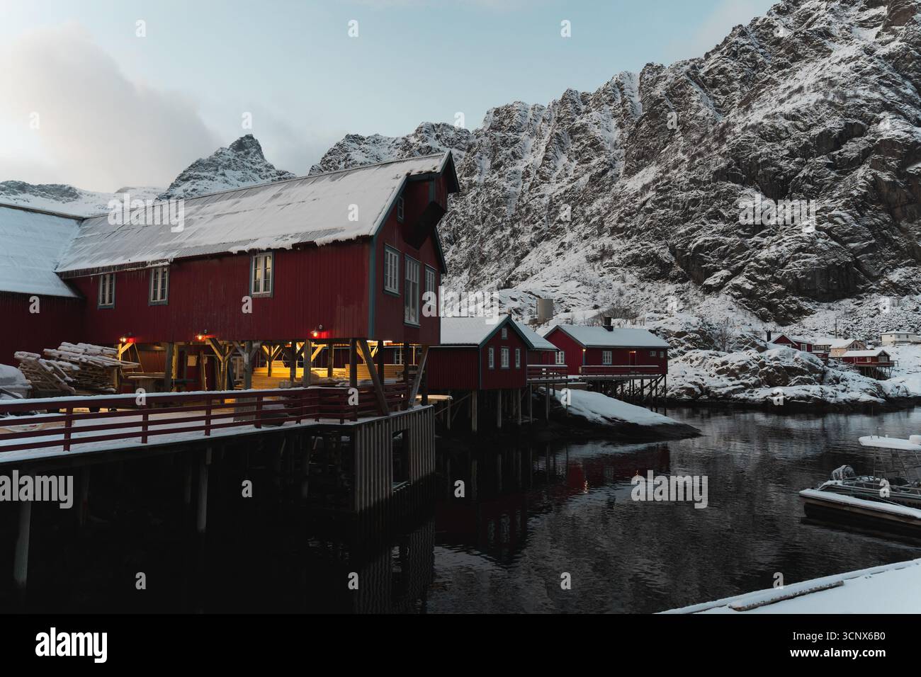Snow dusted red cabins reflect in calm waters beneath towering, rugged ...