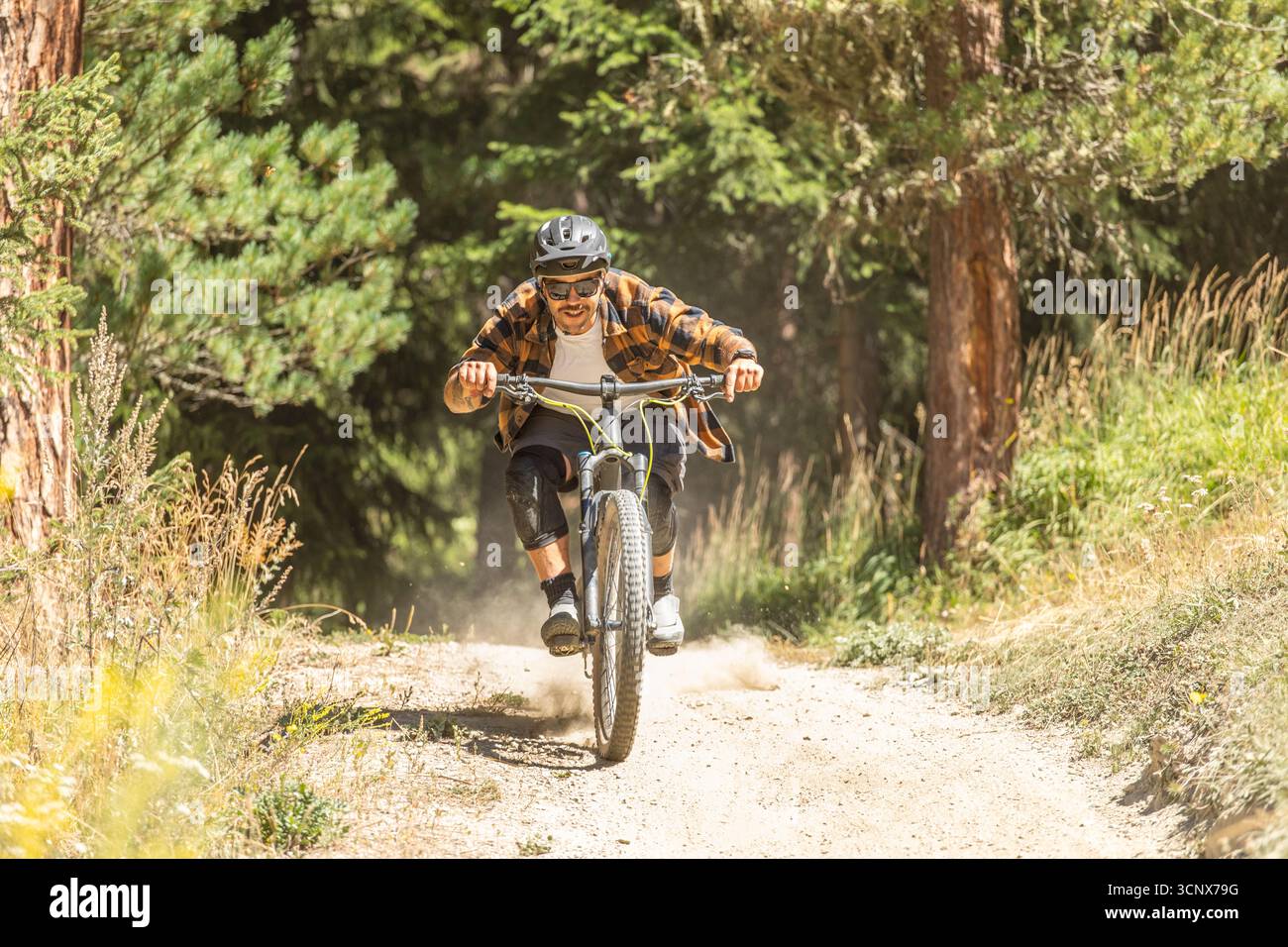 A focused mountain biker wearing a helmet and flannel shirt rides powerfully up a dusty trail ...