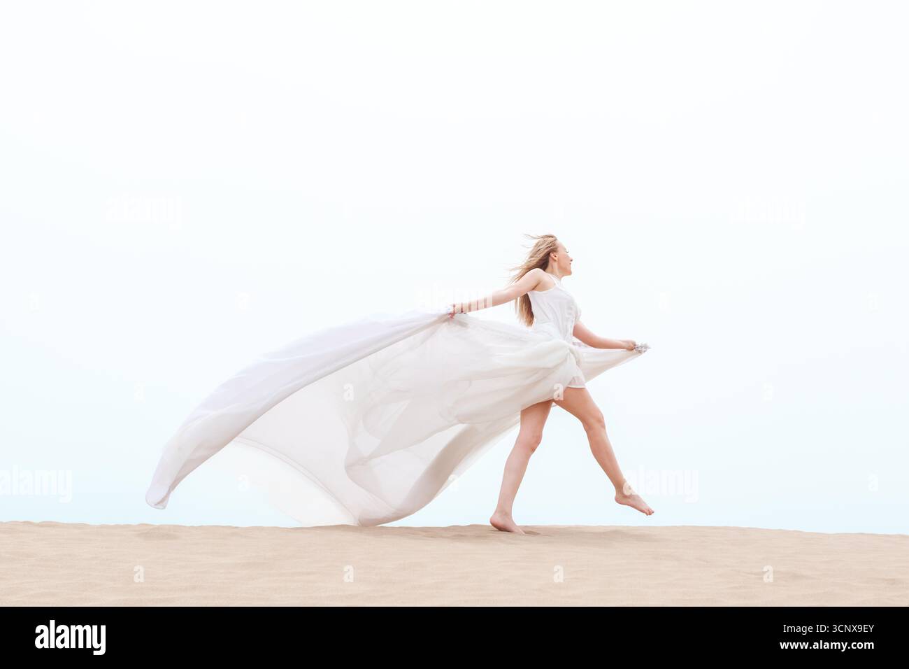 An elegant young woman in a flowing white dress dances gracefully on ...