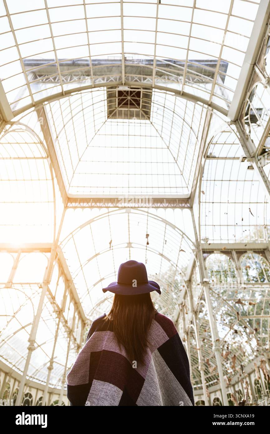 A woman stands under a grand glass ceiling, her back facing the camera ...