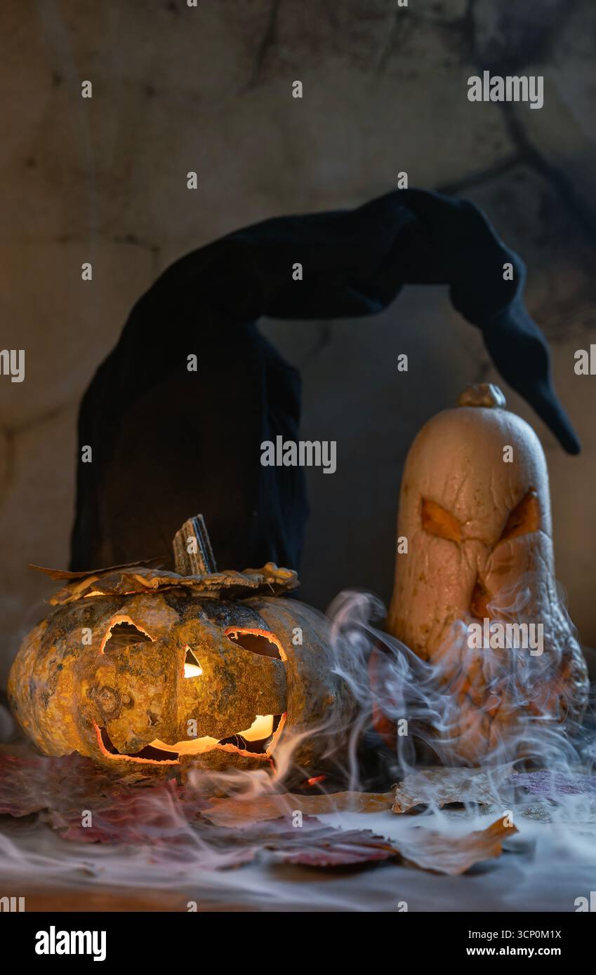 Two carved pumpkins with witch hats and autumn leaves shrouded in smoke ...