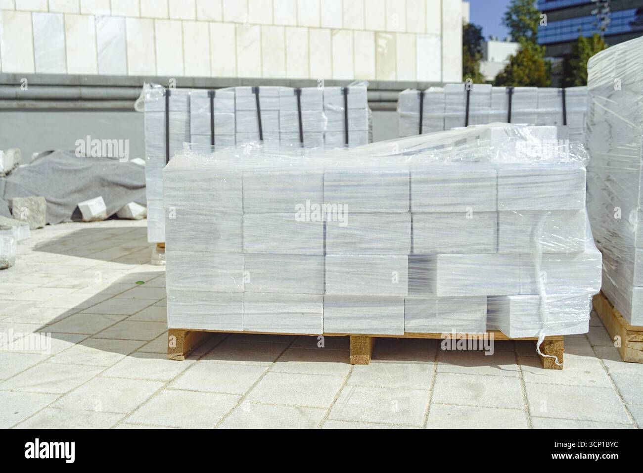 Cut natural stone tiles stacked on wooden pallets. White square blocks ...