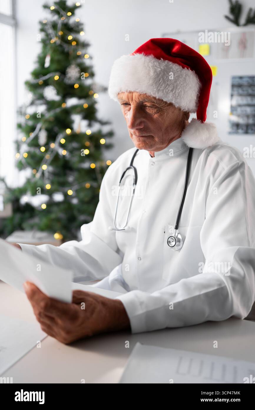 Decorated office in Christmastime. Old male doctor reading paper ...