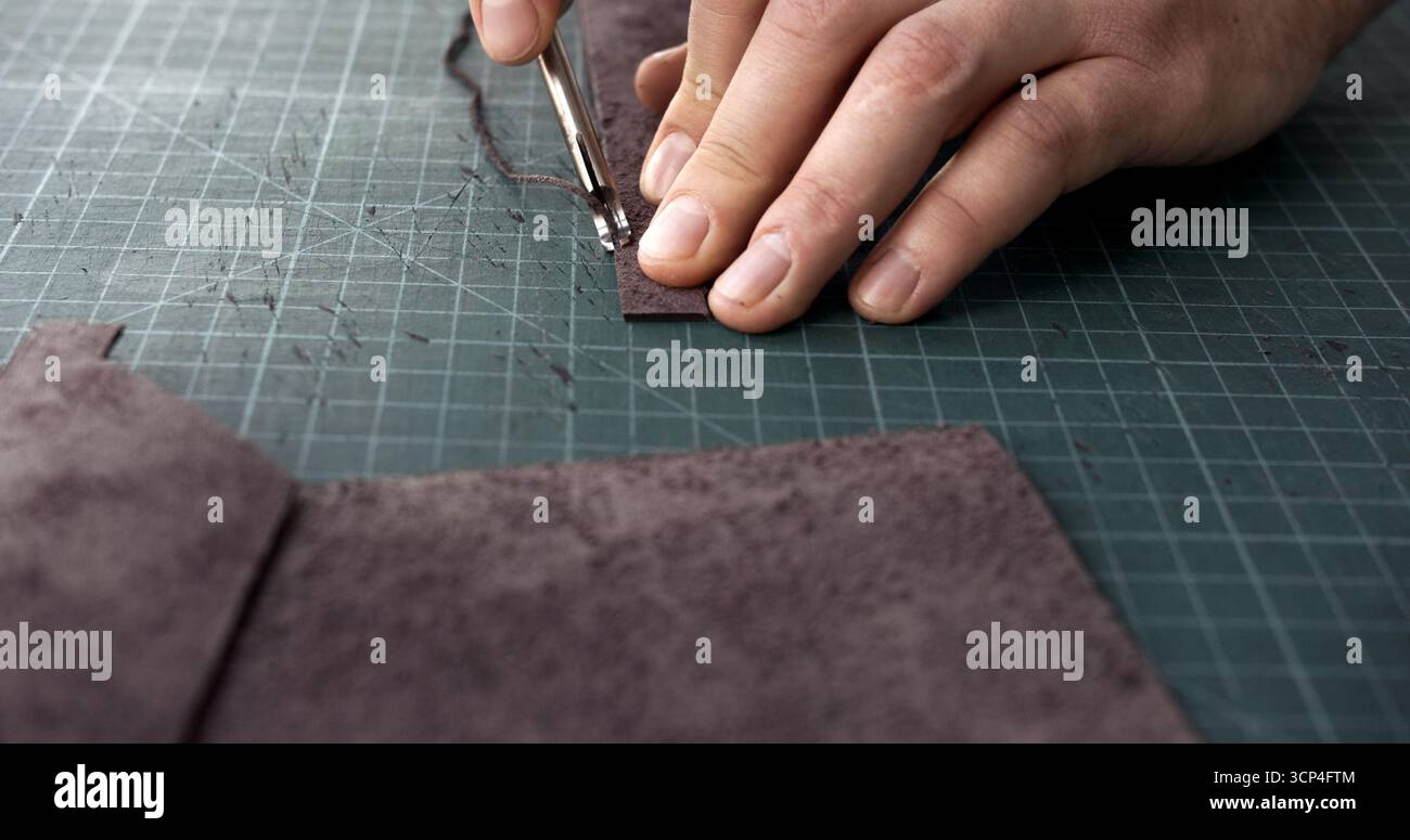 Craftsman using edge tool on leather strip for handmade leather goods ...