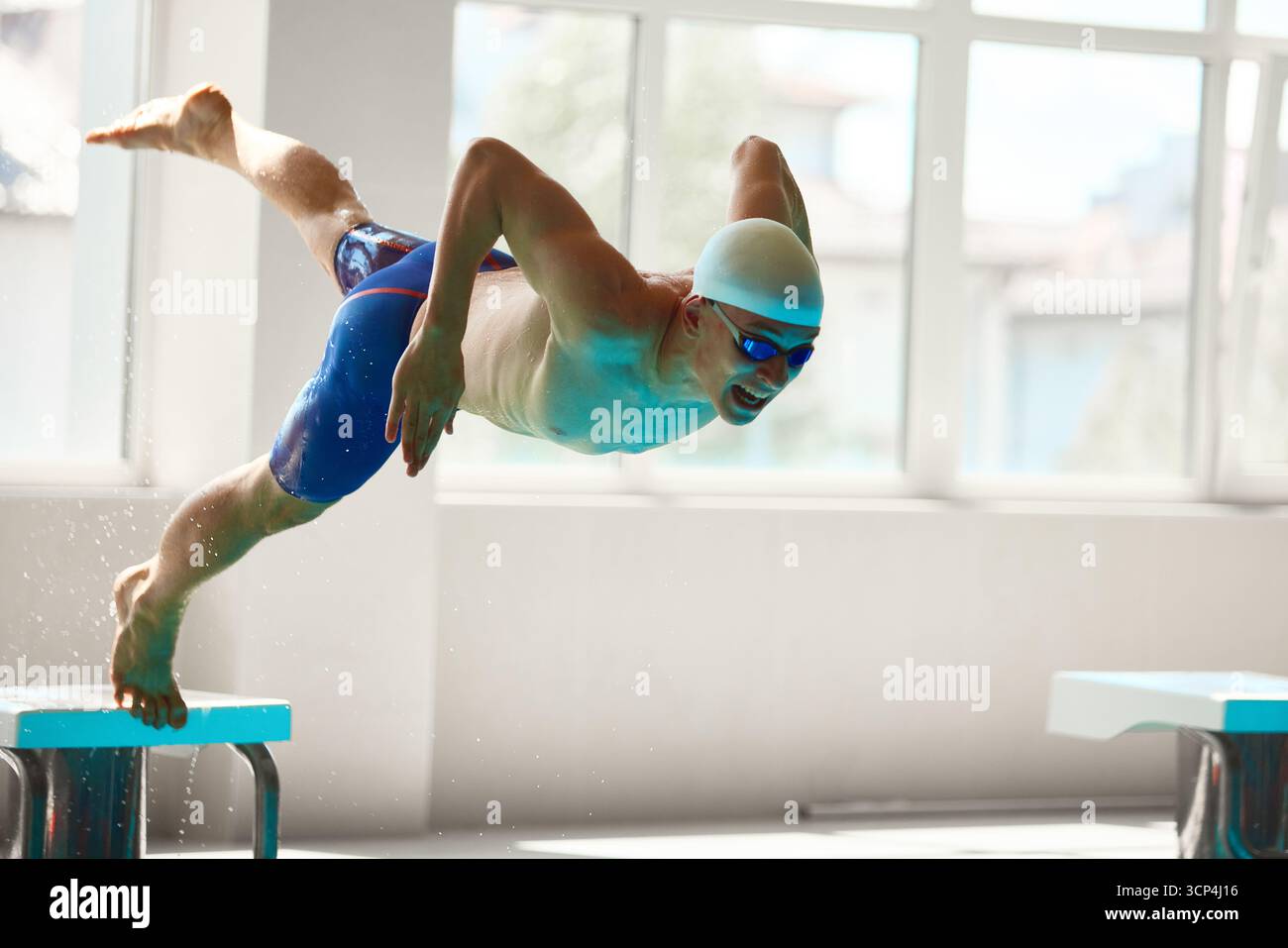 Focused male swimmer diving from block with determination in indoor ...