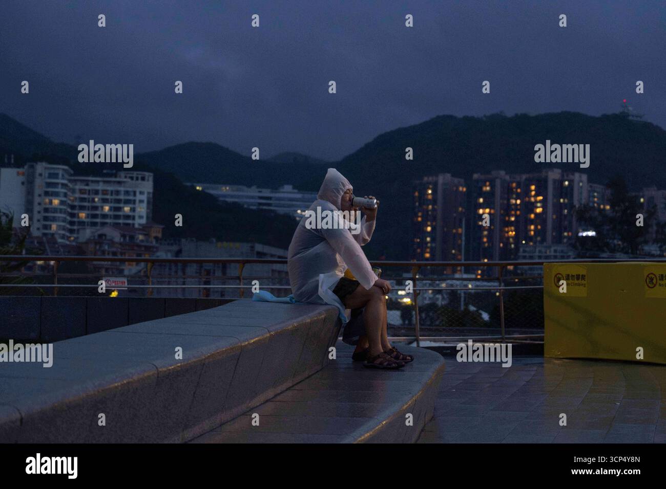 An man drinks a beer as he watches waves crashing on a beach in the ...