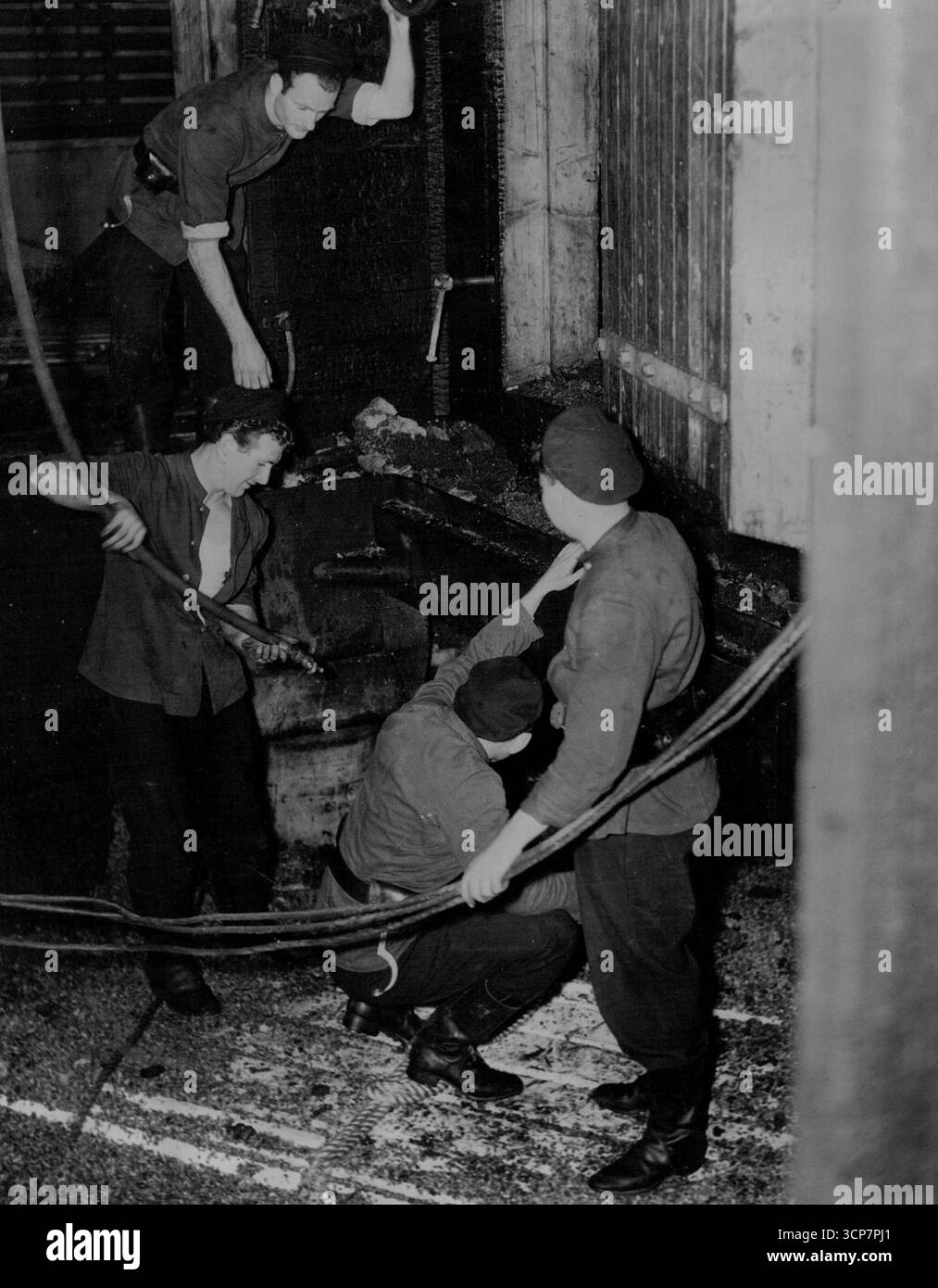 Firemen at work in no 3 hold where the fire started. They are standing ...