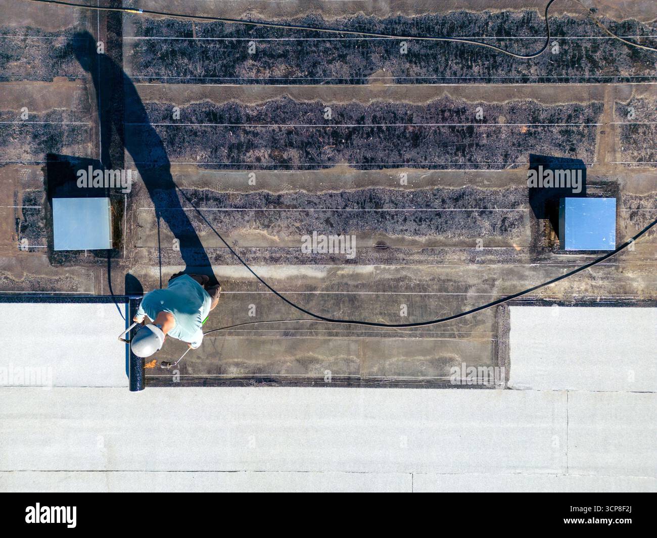 A roofer torches a membrane layer on a flat roof using a tiger torch to ...