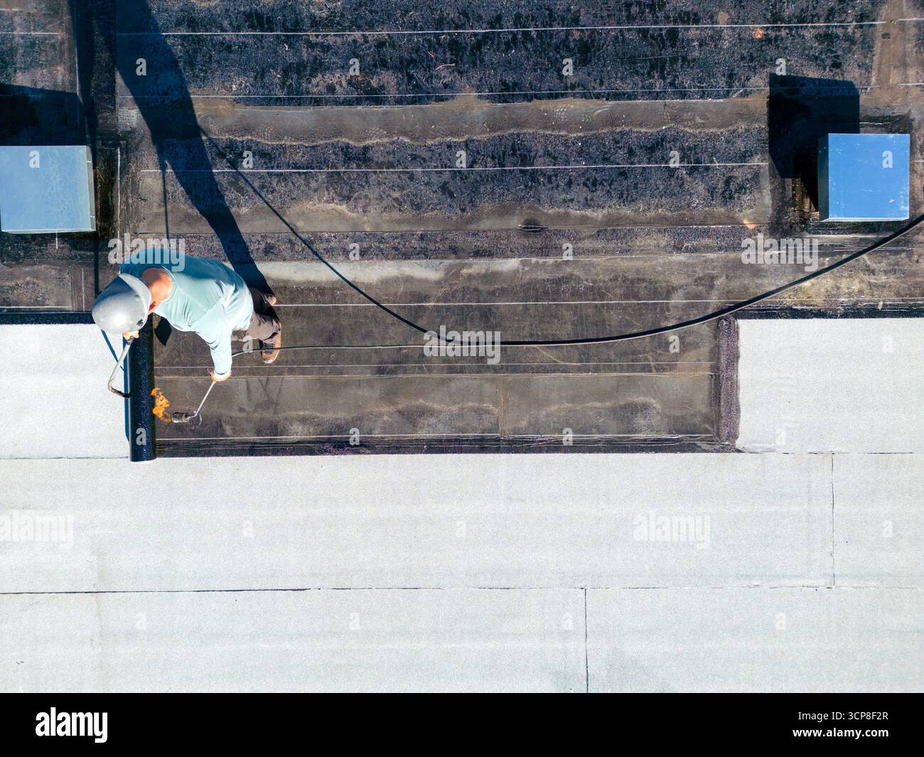 A roofer torches a membrane layer on a flat roof using a tiger torch to ...