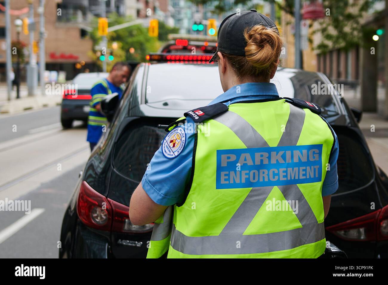 A parking enforcement officer writes a ticket for a car as it gets ...