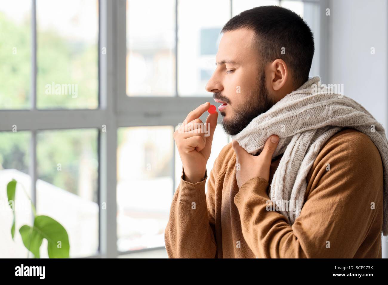 Ill young man taking throat lozenge at home Stock Photo - Alamy