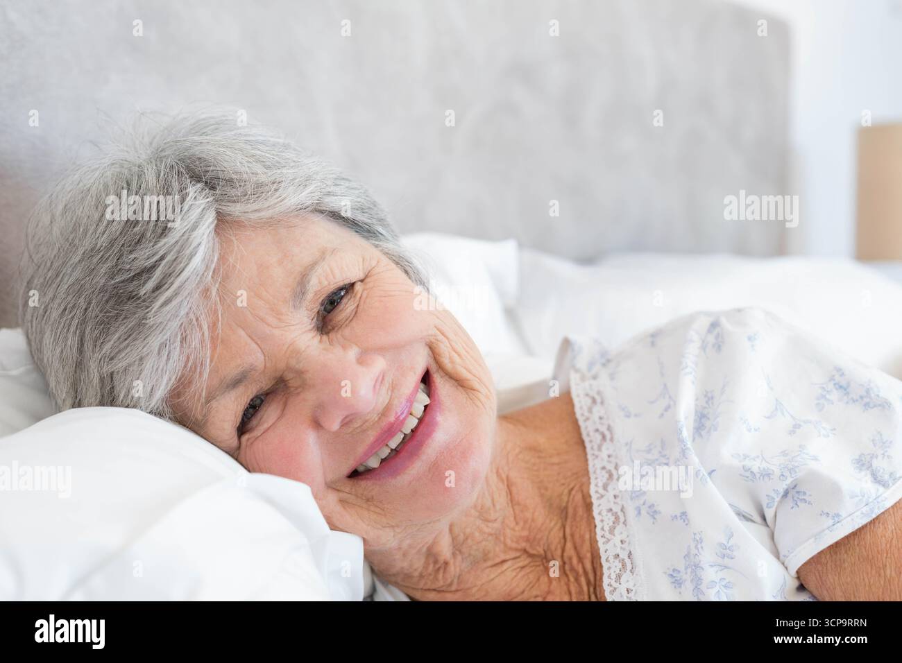 Senior woman reclining in bedroom, resting head on pillow by gray ...