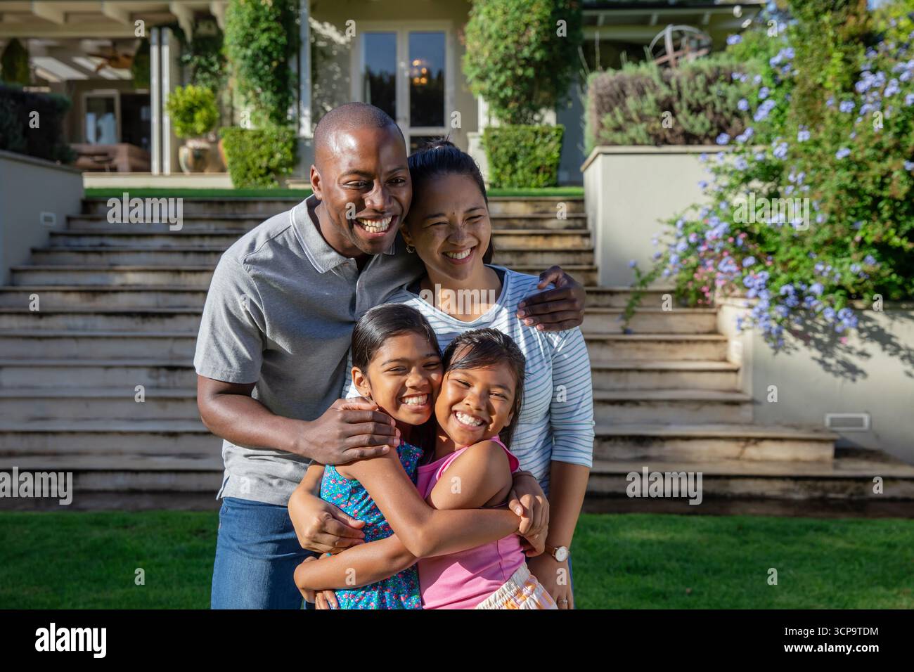 Diverse family hugging together on grass lawn in front yard near stone ...