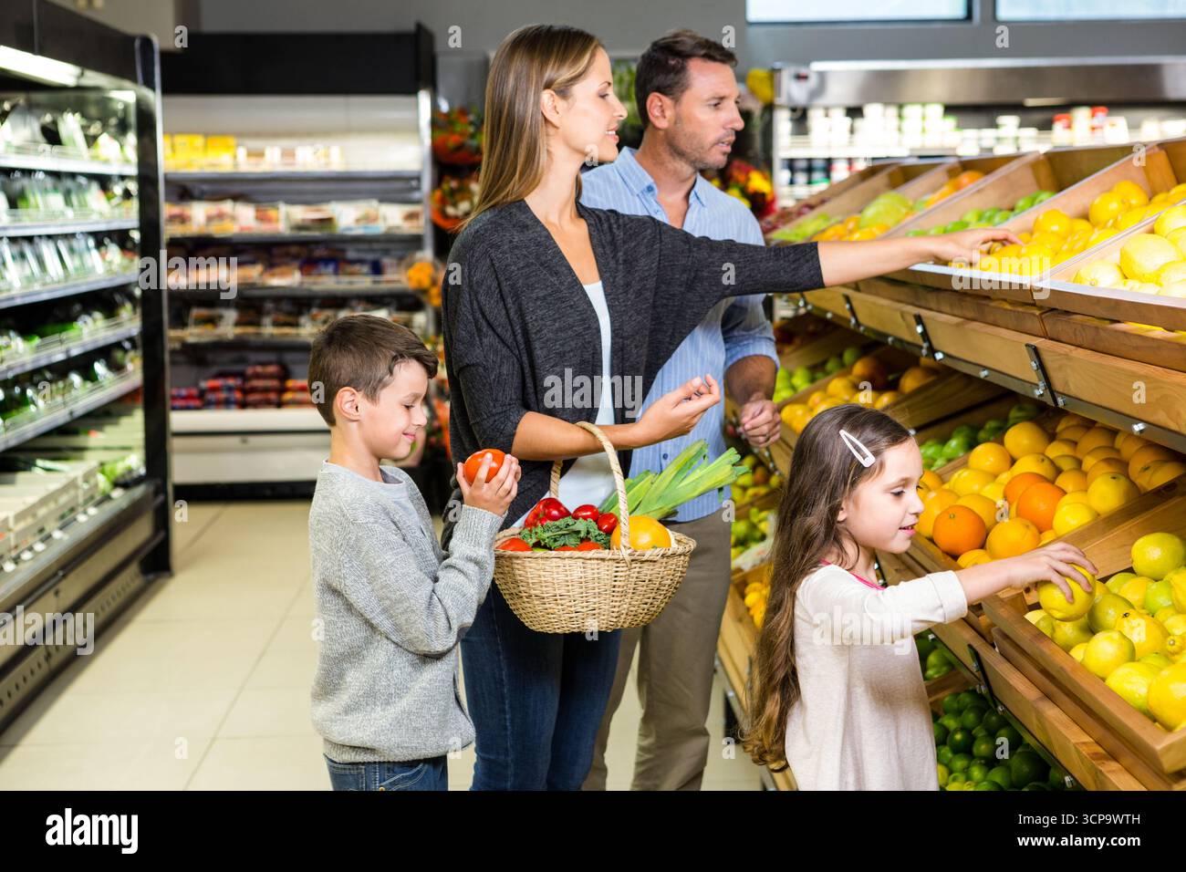 Family of four shopping in supermarket produce aisle holding wicker ...