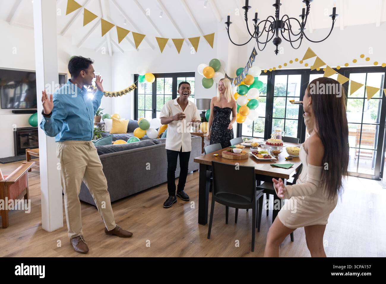 Diverse friends gathering around dining table laughing and pointing at cake in living room Stock ...