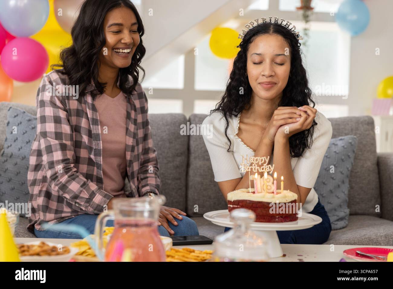 Diverse mom and teenage daughter making birthday wish on couch in ...