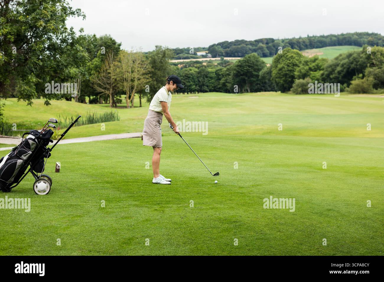 Senior female golfer standing on fairway addressing golf ball with club ...