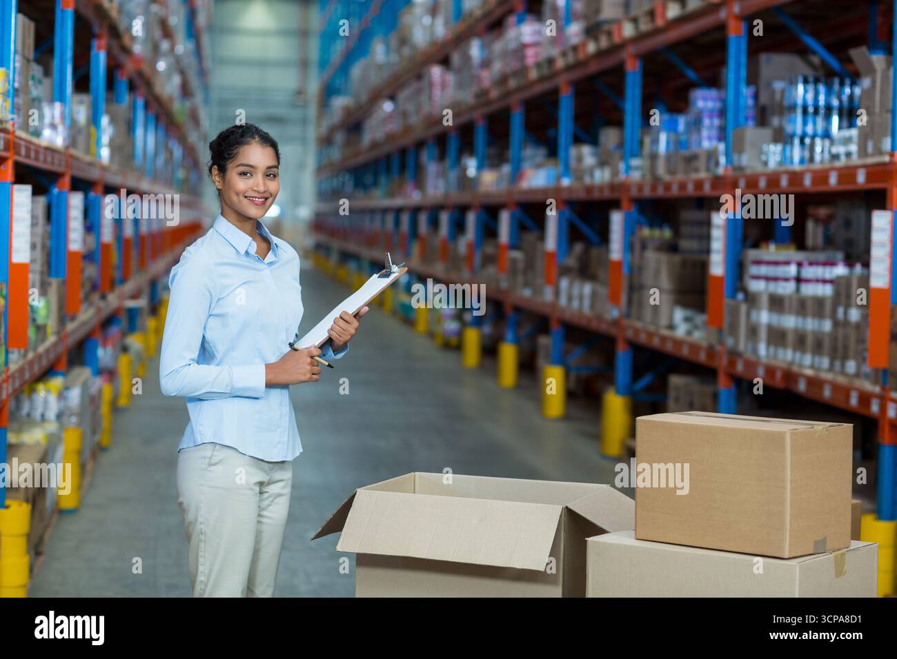 Inventory supervisor checking clipboard scanning boxes on aisle flanked ...